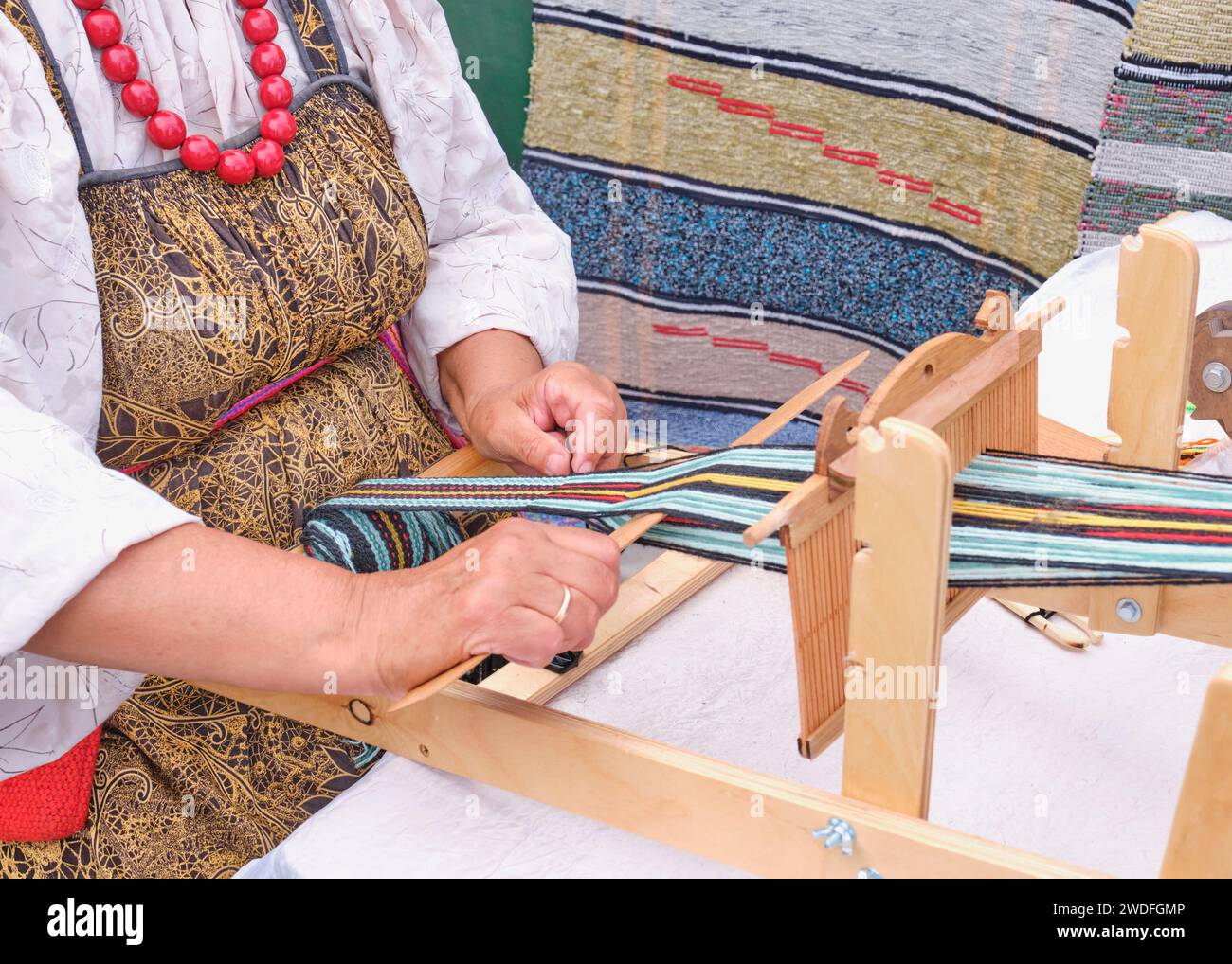 Hands of senior white woman weaving colorful striped decorative band on ...