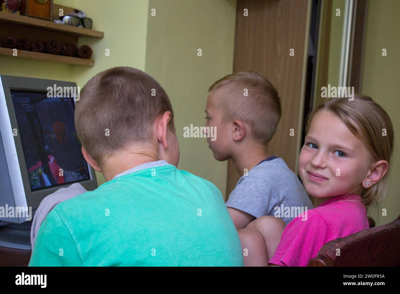 a family of children sitting behind a computer desk and playing games ...