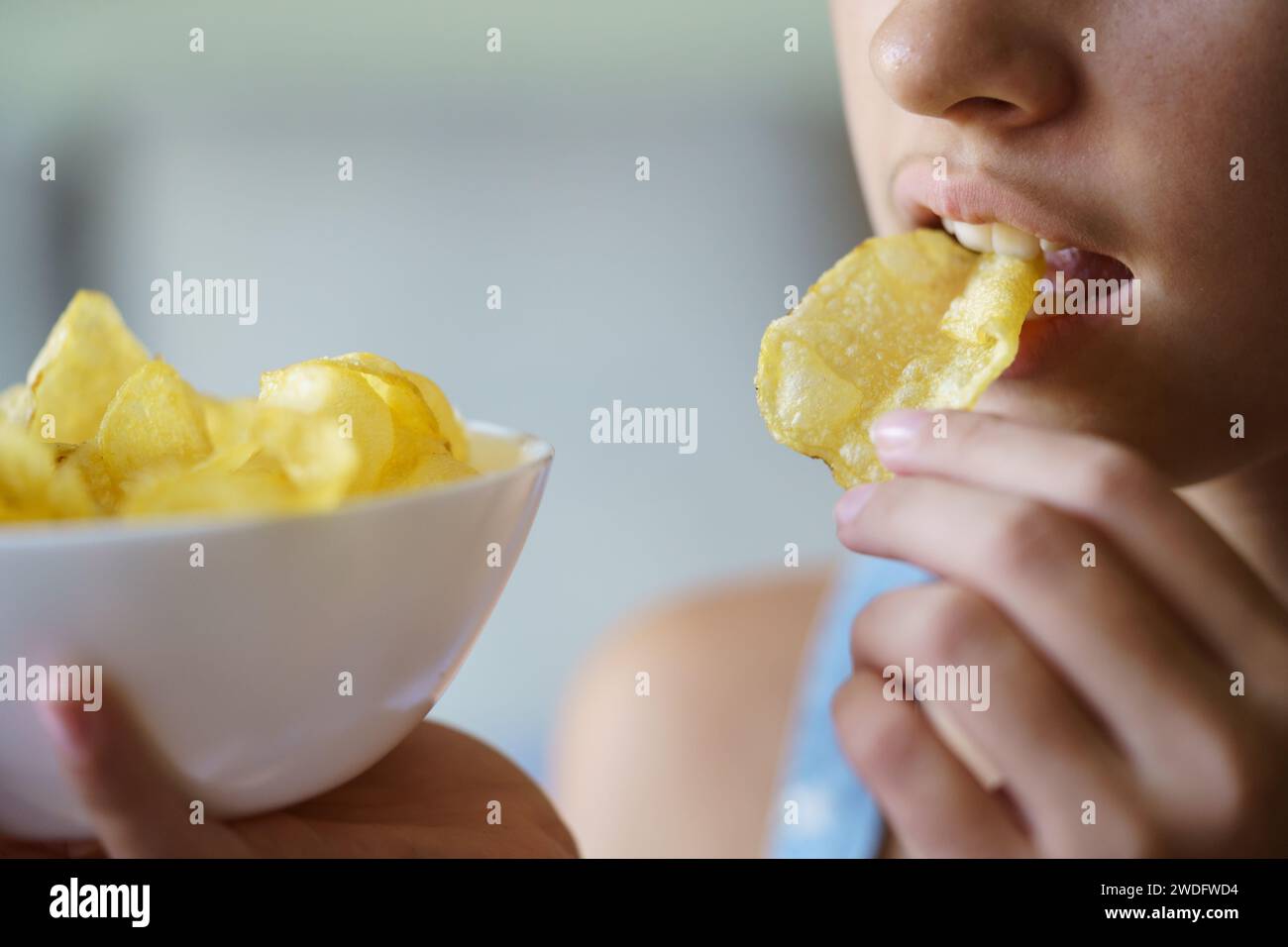Crop teenage girl eating crispy potato chip while holding bowl Stock ...