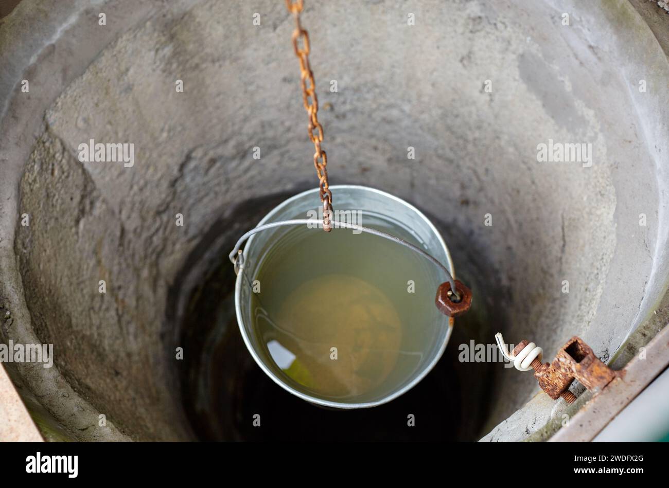 Metal bucket at draw-well in European village. Retro stone water well ...