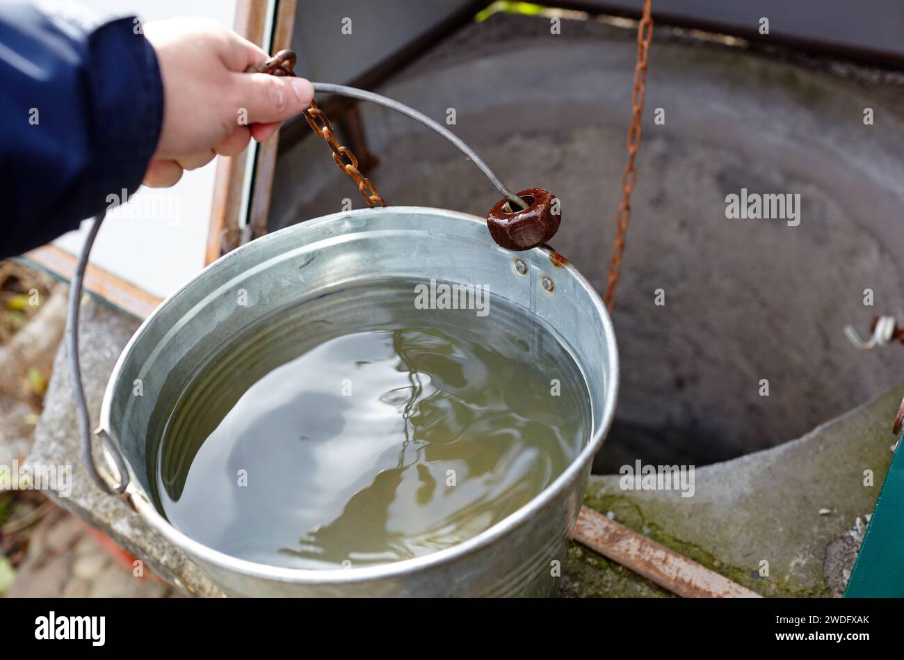 Man hand holding metal bucket with fresh water. Water from a deep well ...