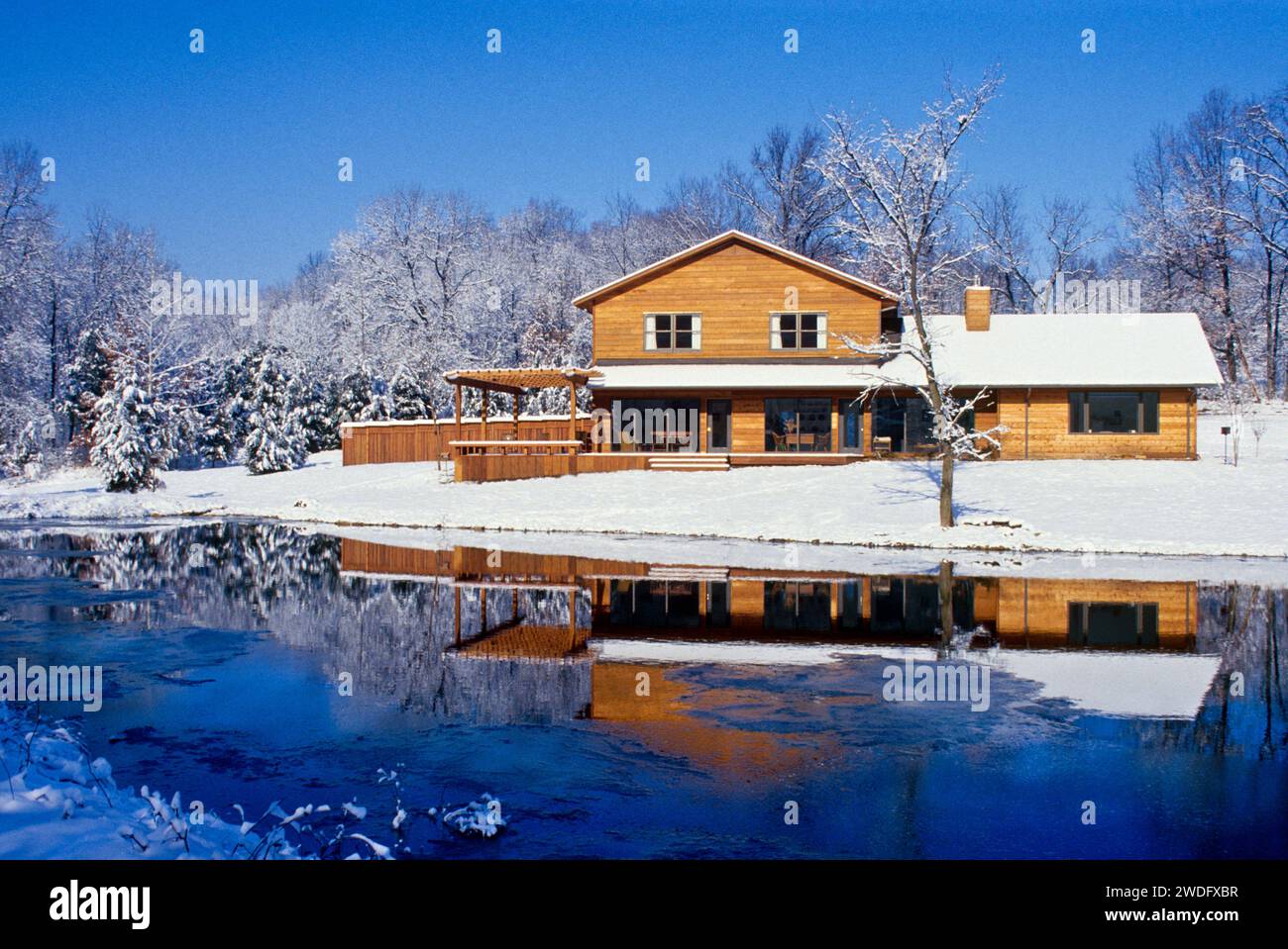 A cedar home reflected in an ice covered lake in an early spring sunny ...