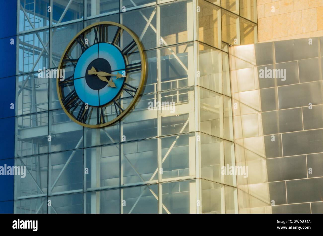 A large clock on the glass facade of a building reflecting the golden ...