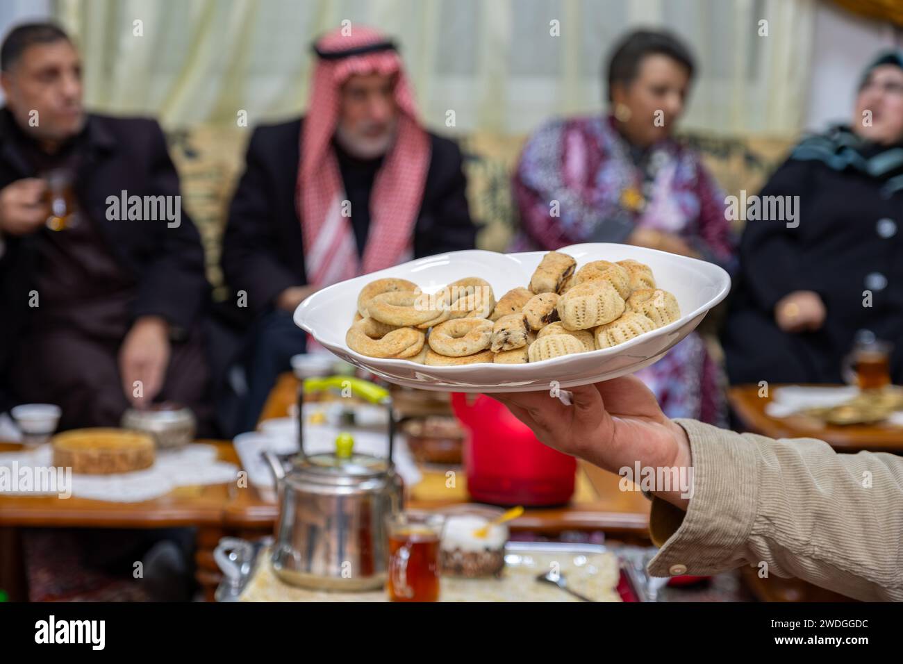 Hand holding Eid sweets amidst a family gathering. Signifying warmth ...