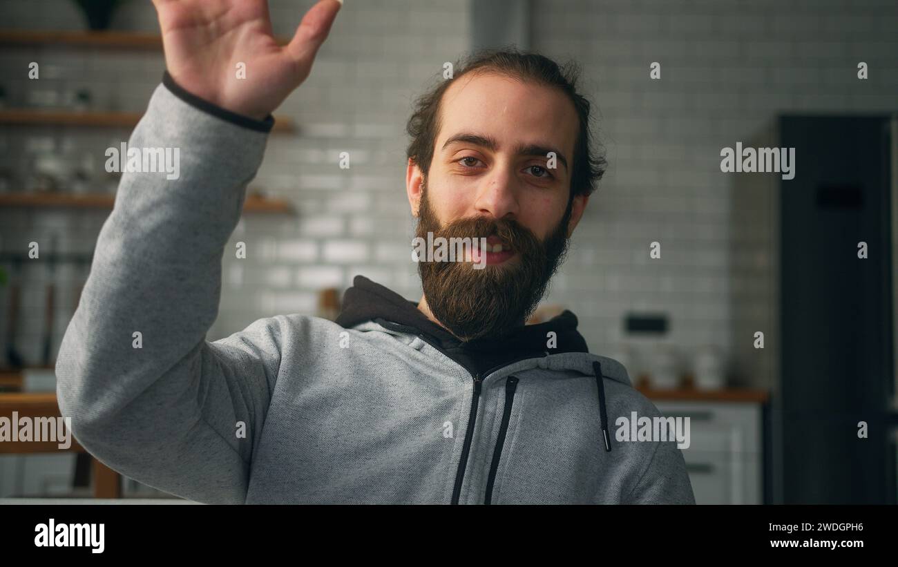 Bearded man sitting on sofa at home with kitchen background, looking at ...