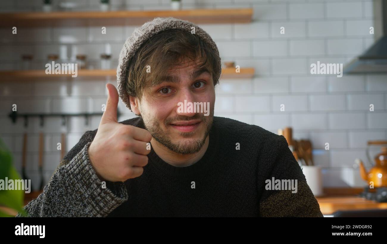 Portrait of young man with beanie sitting in modern kitchen at home ...
