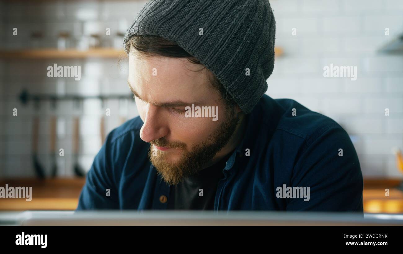 Young businessman with beanie working at home in the kitchen with his ...