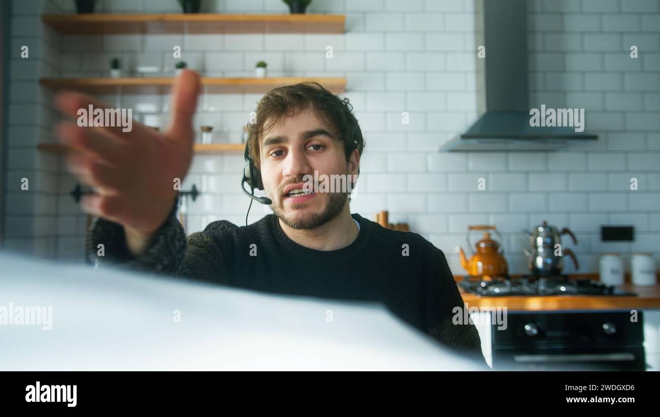 Young angry manager man with wireless headset sitting in modern kitchen ...