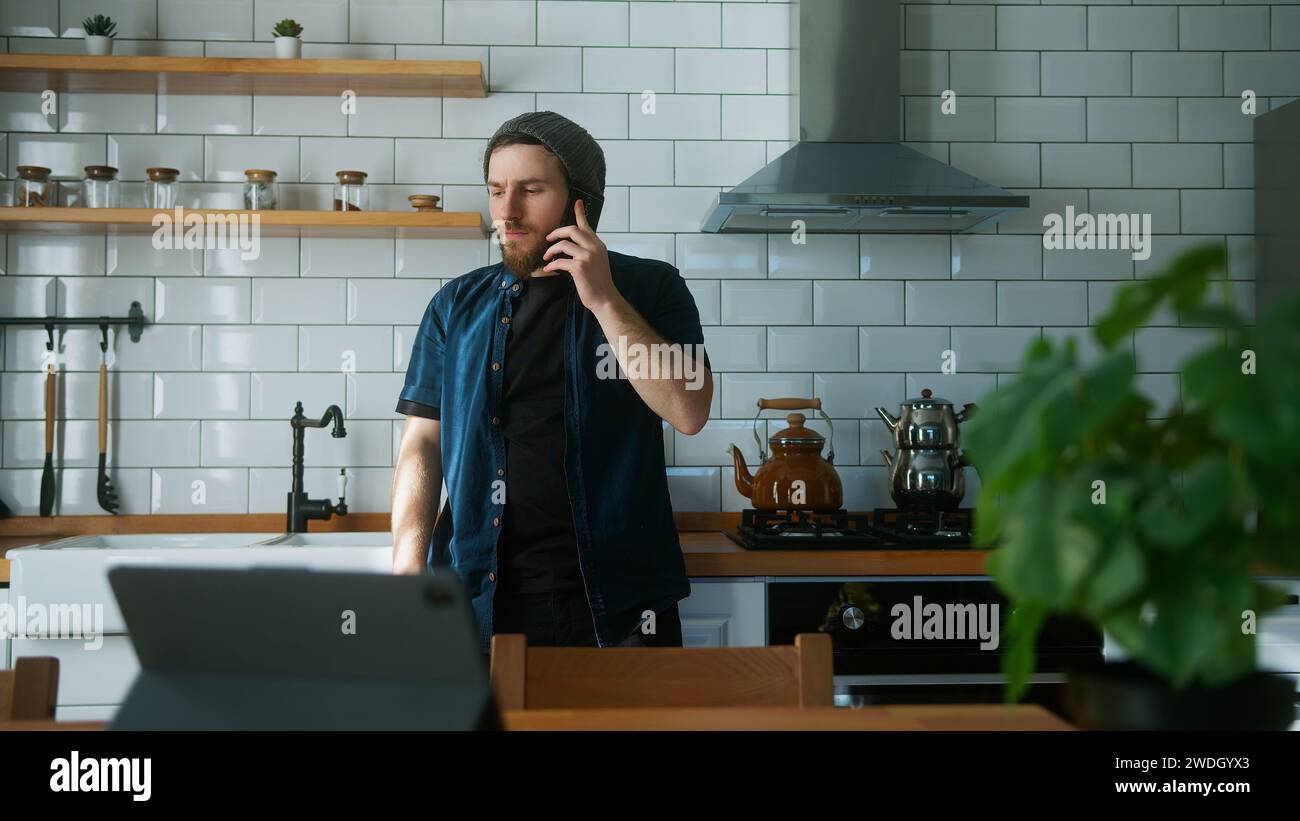 Handsome young adult man talking on the phone in modern kitchen at home ...