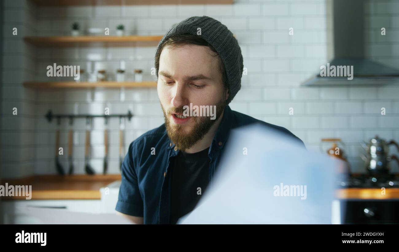 Young angry manager man with beanie sitting in modern kitchen at home ...