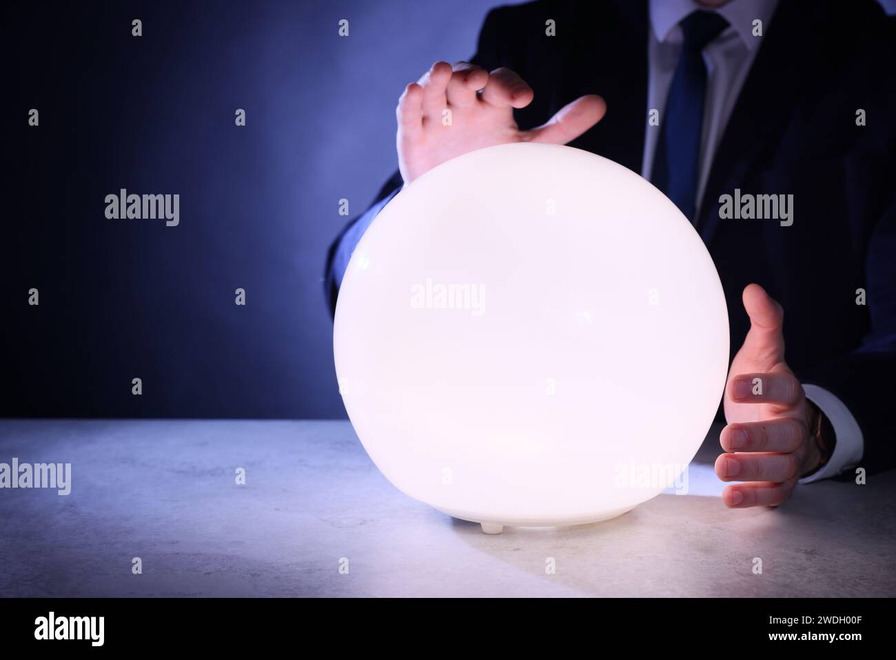 Businessman using glowing crystal ball to predict future at table ...