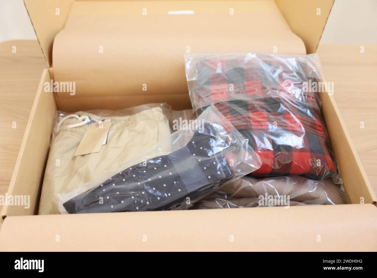 Open cardboard box with different clothes in plastic bags on wooden ...