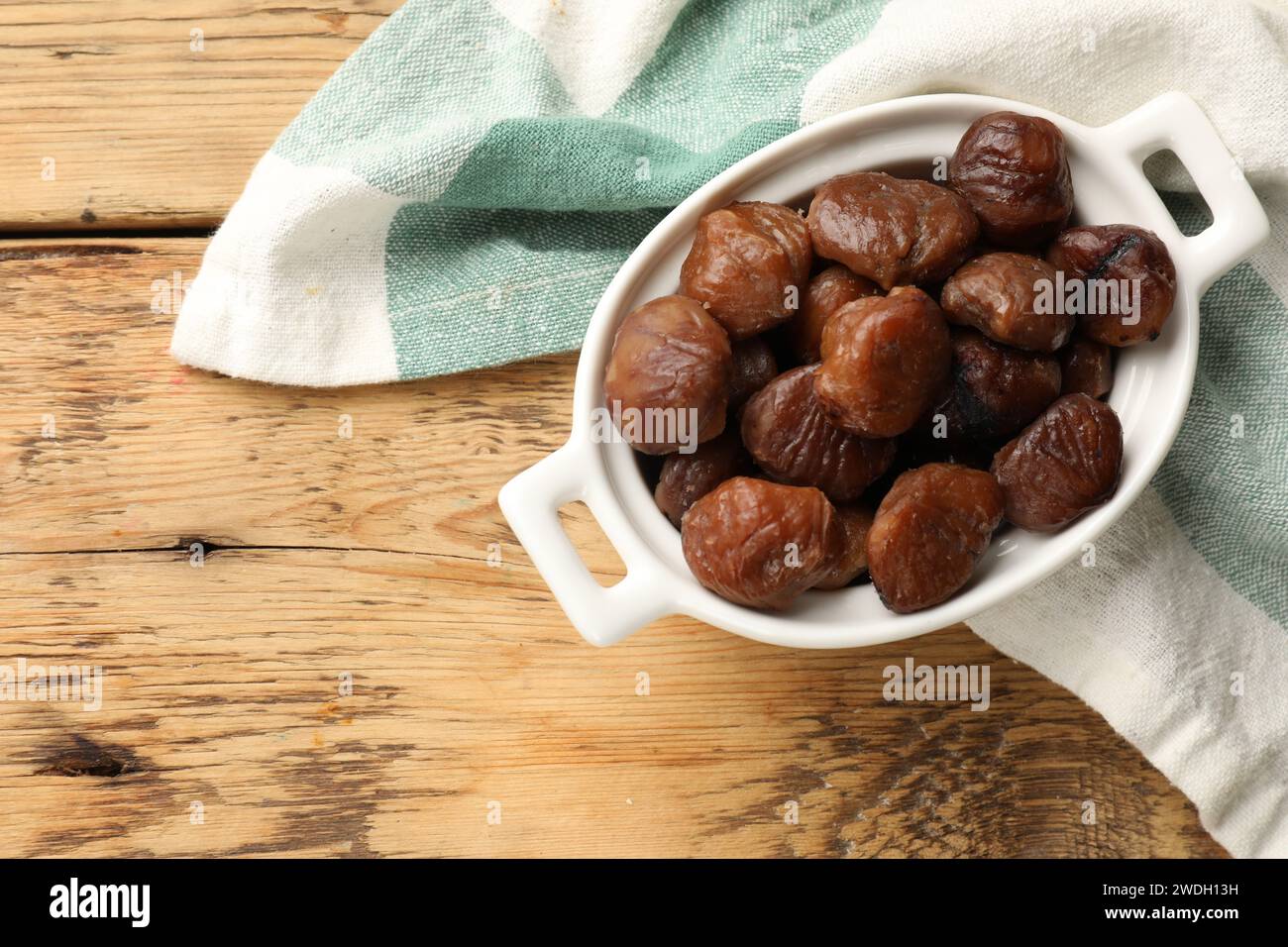 Roasted edible sweet chestnuts in dish on light wooden table, top view ...