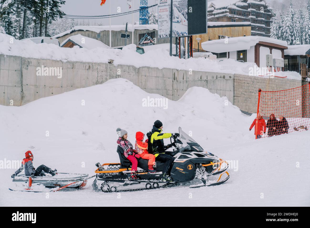 Dad and children ride on a snowmobile with a sled attached to the back ...