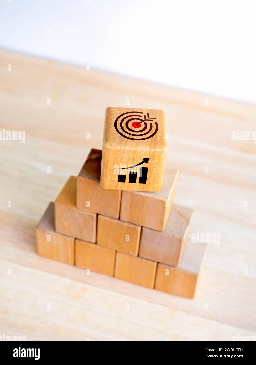 Target icon and growth graph symbol on top of wooden cube blocks stack as pyramid shape on white ...