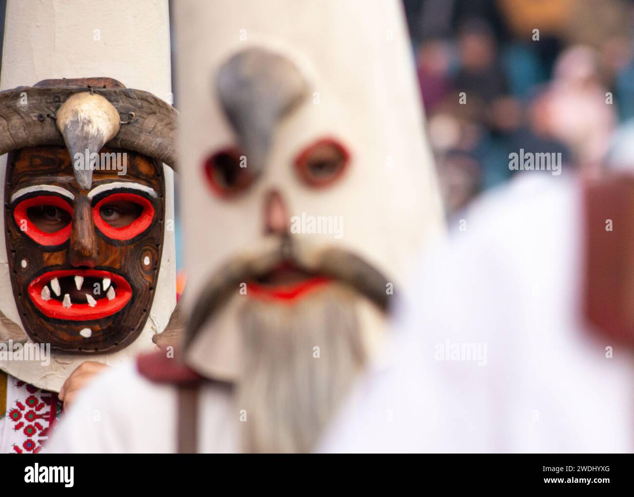 Kukeri dancers in white outfit with distinctive tall conical mask and their eyes seen through ...