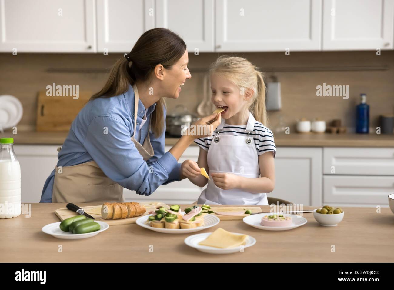 Cheerful mom feeding cute preschool kid girl while cooking Stock Photo ...