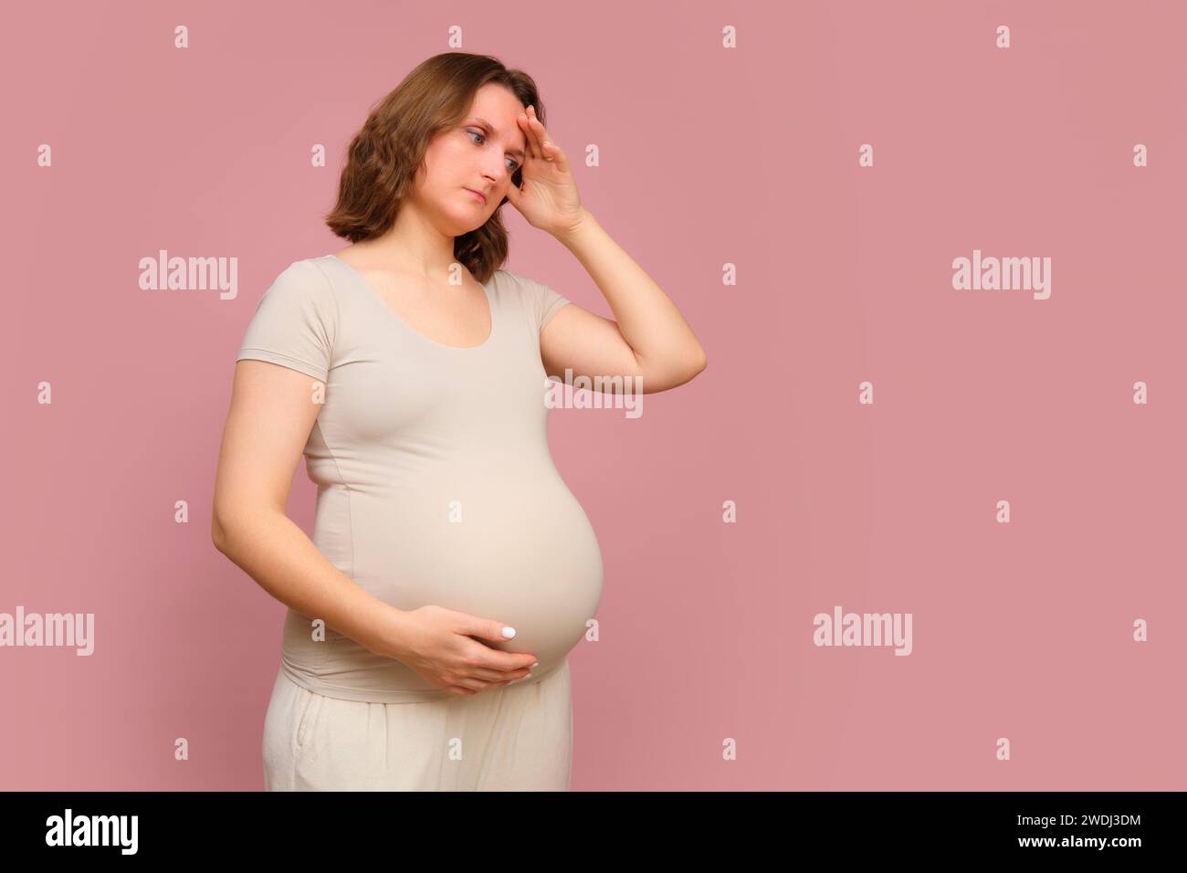 A sad pregnant woman on a pink studio background. Pregnancy in a ...