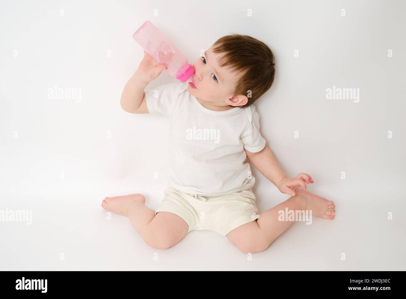 Happy baby drinks milk from bottle on studio white background. Resting ...