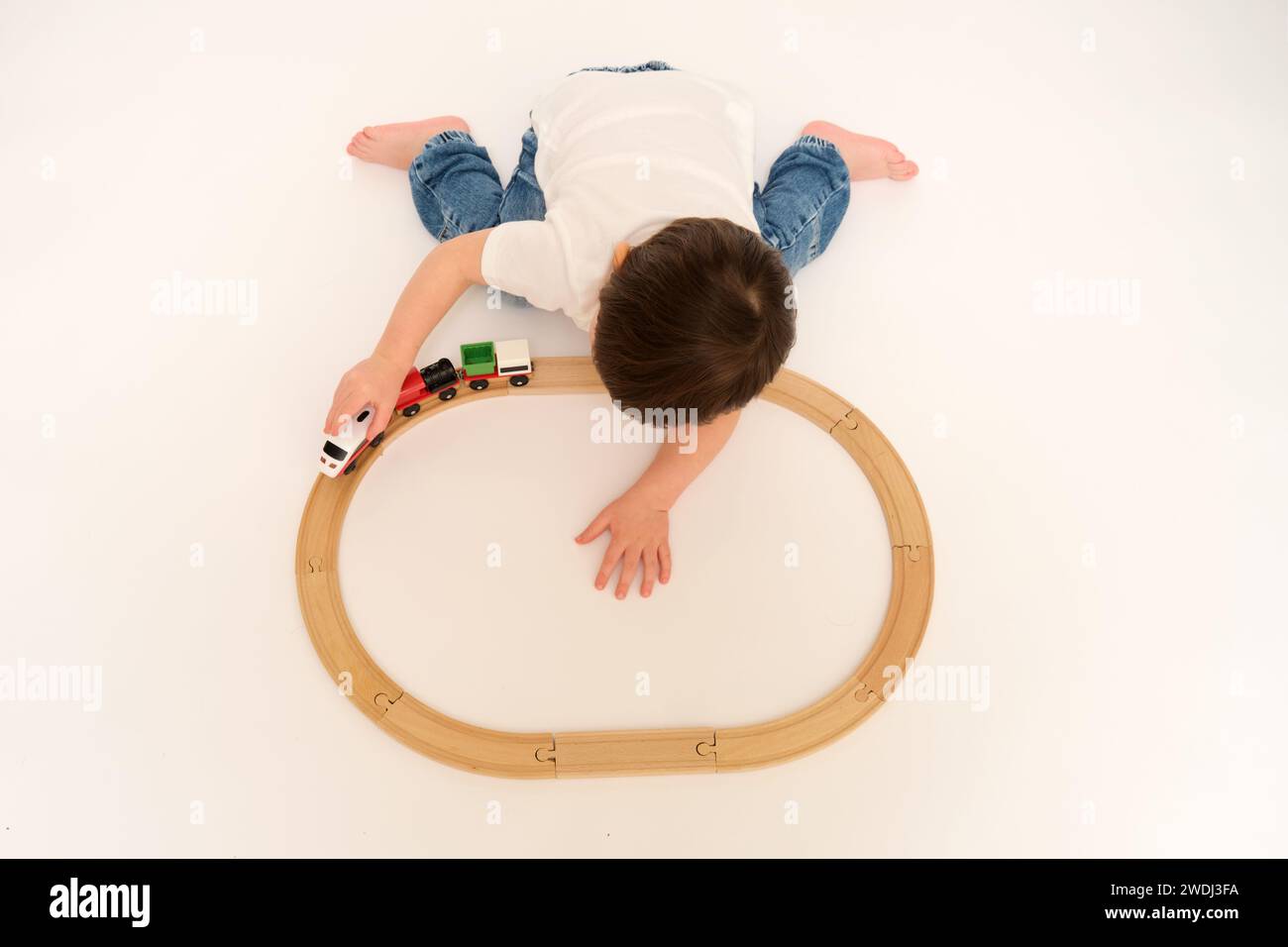 Toddler baby is playing train cars on the railroad, studio white ...