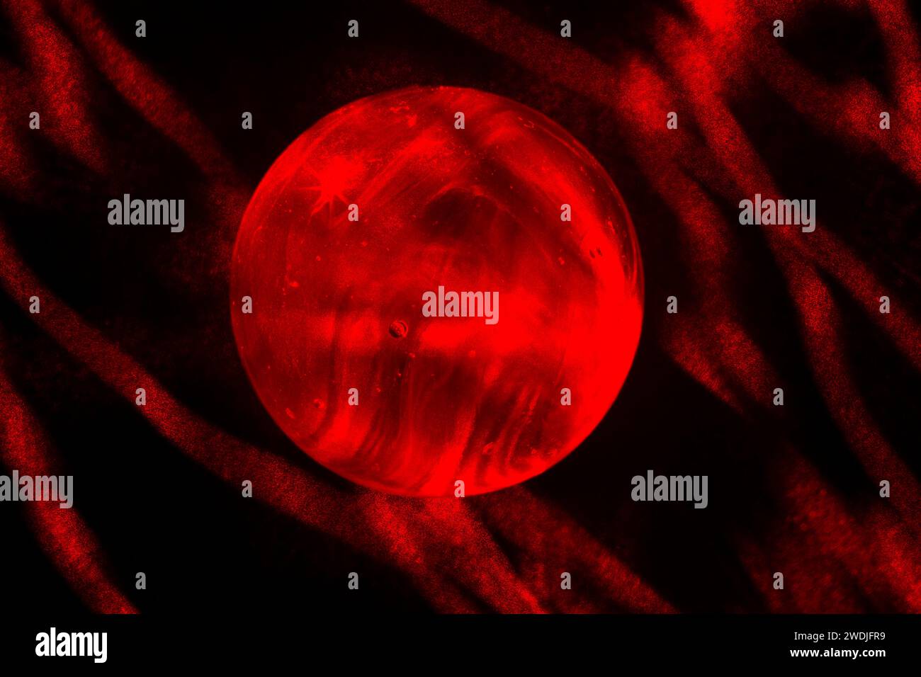A red glass marble on black background light painted with red laser ...