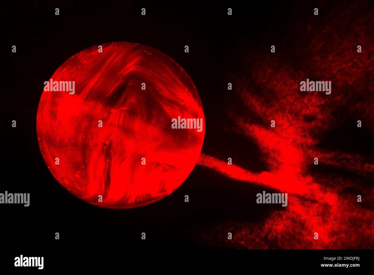 A red glass marble on black background light painted with red laser ...