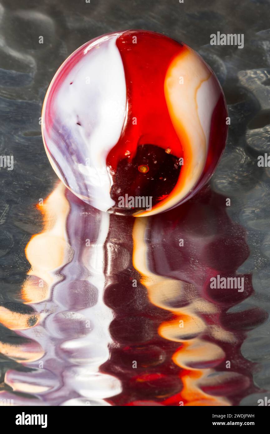A red and white swirl glass marble in a reflective metal bowl Stock ...