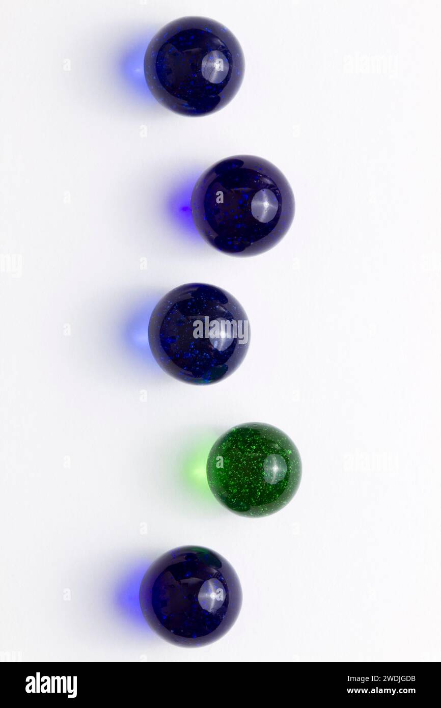 Blue marbles with one green marble staggered in a row Stock Photo - Alamy