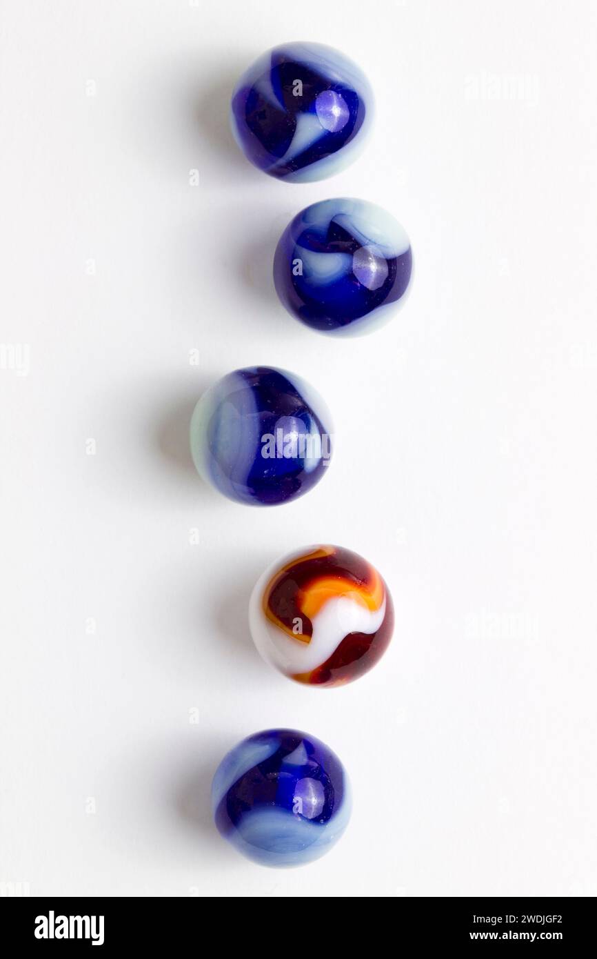 Blue marbles with one red marble staggered in a row Stock Photo - Alamy