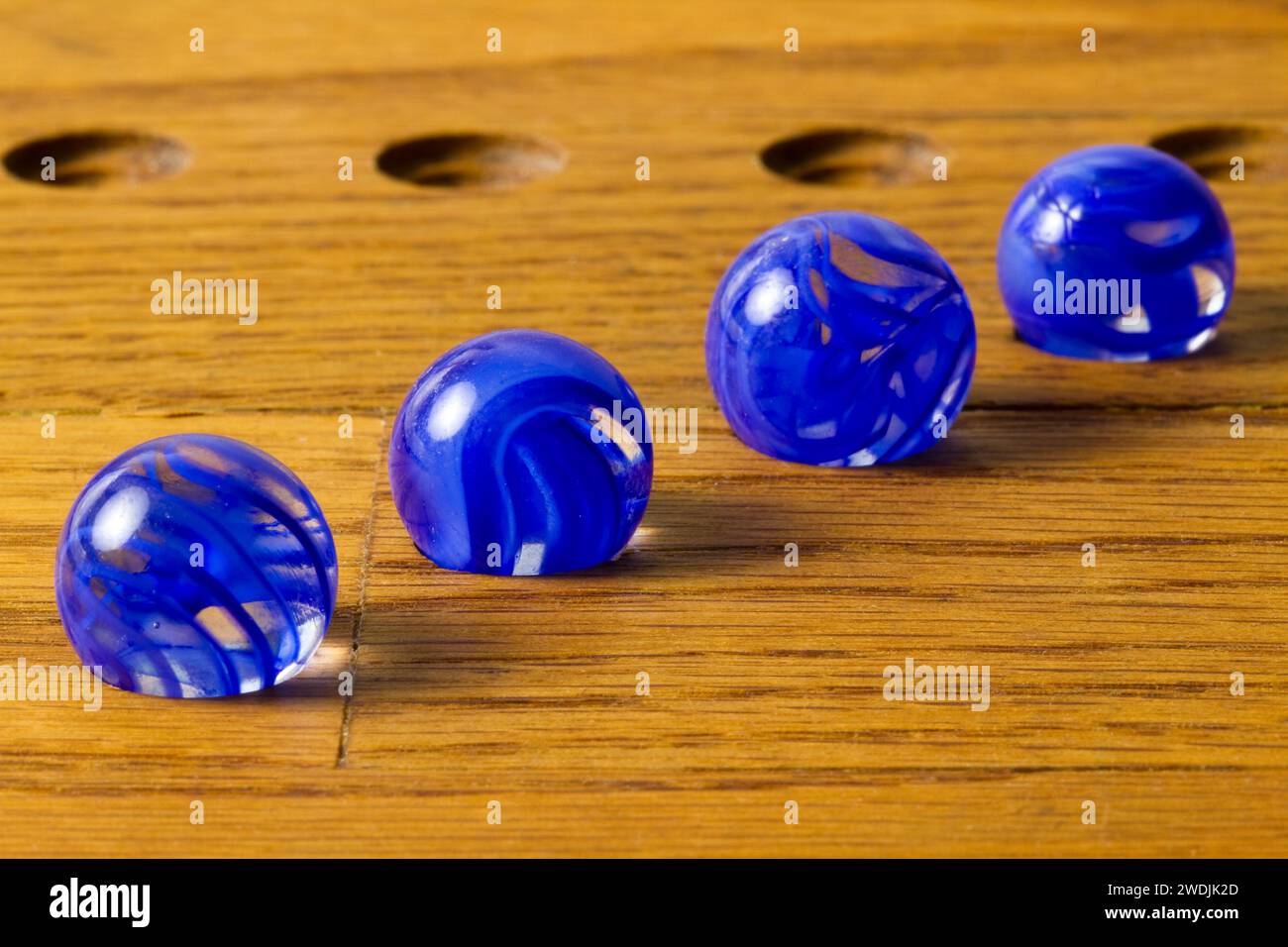 Four blue swirl glass marbles on a wooden game board Stock Photo - Alamy