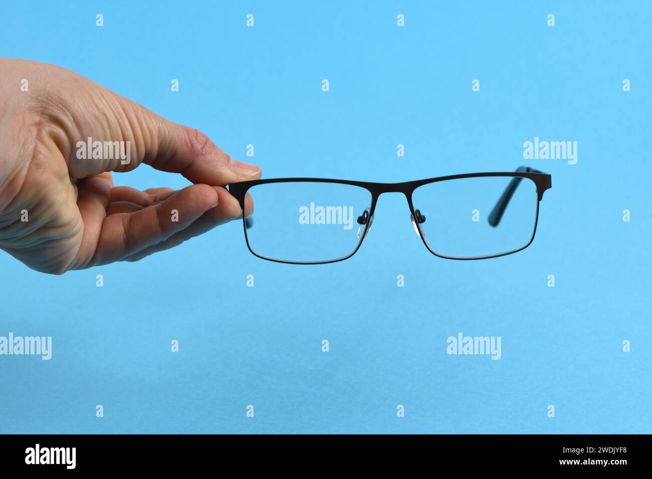 Hand holding plastic black glasses, isolated on blue background. High ...