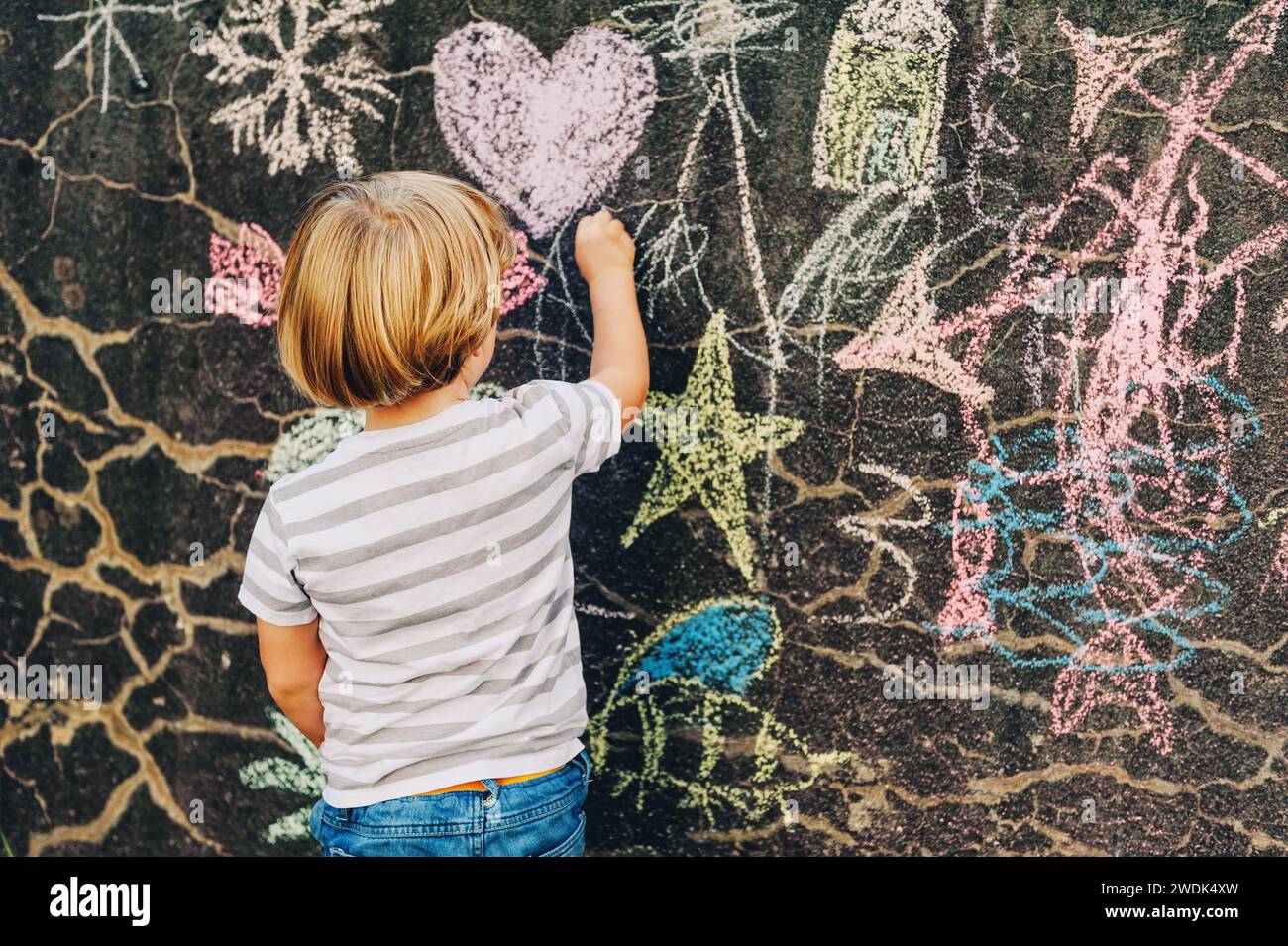 Adorable little boy drawing with a chalk outdoors. Outside activities ...