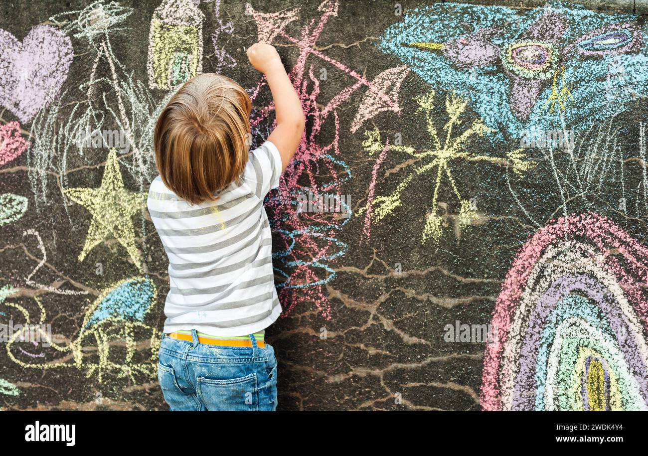 Adorable little boy drawing with a chalk outdoors. Outside activities ...