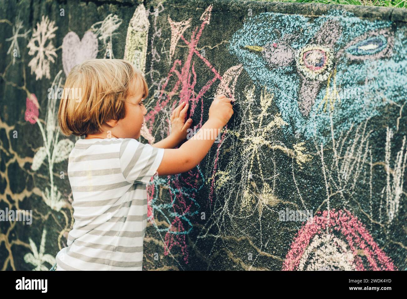 Adorable little boy drawing with a chalk outdoors. Outside activities ...