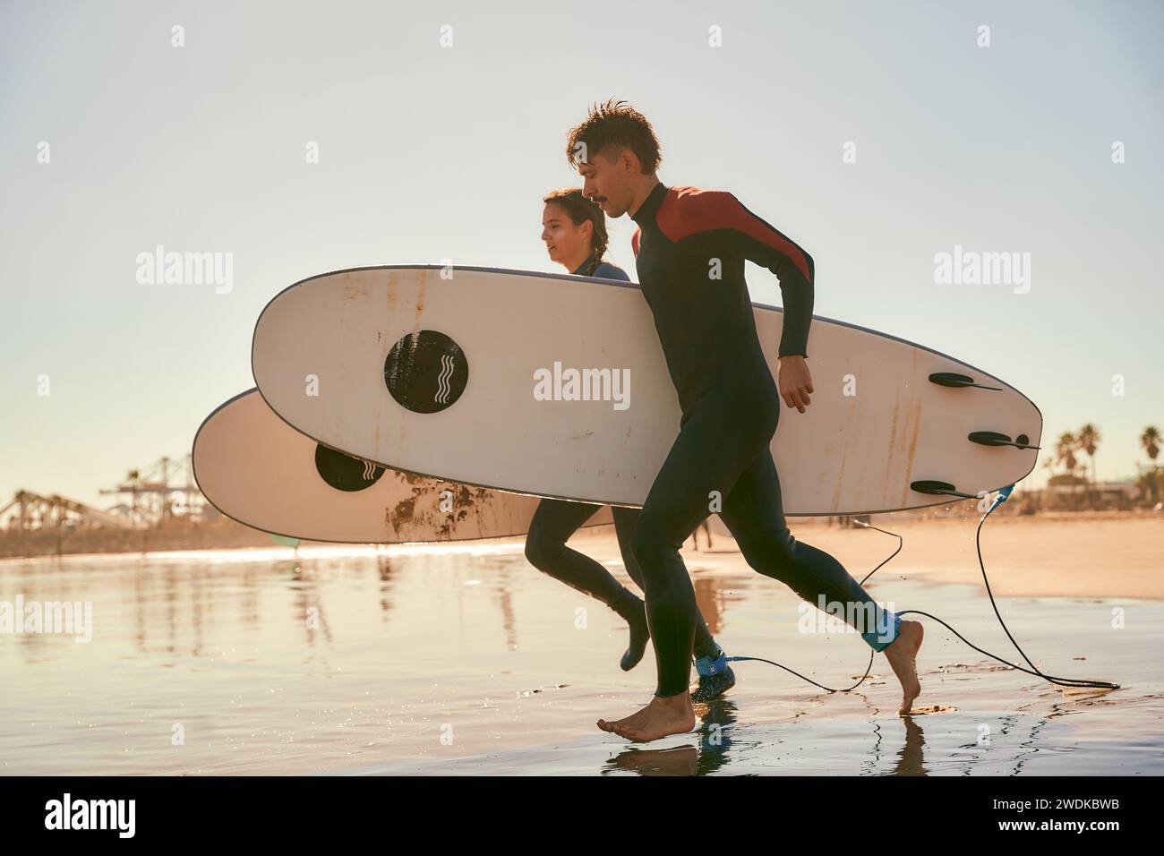 Side view of surfers running into the sea holding surfboards. High ...