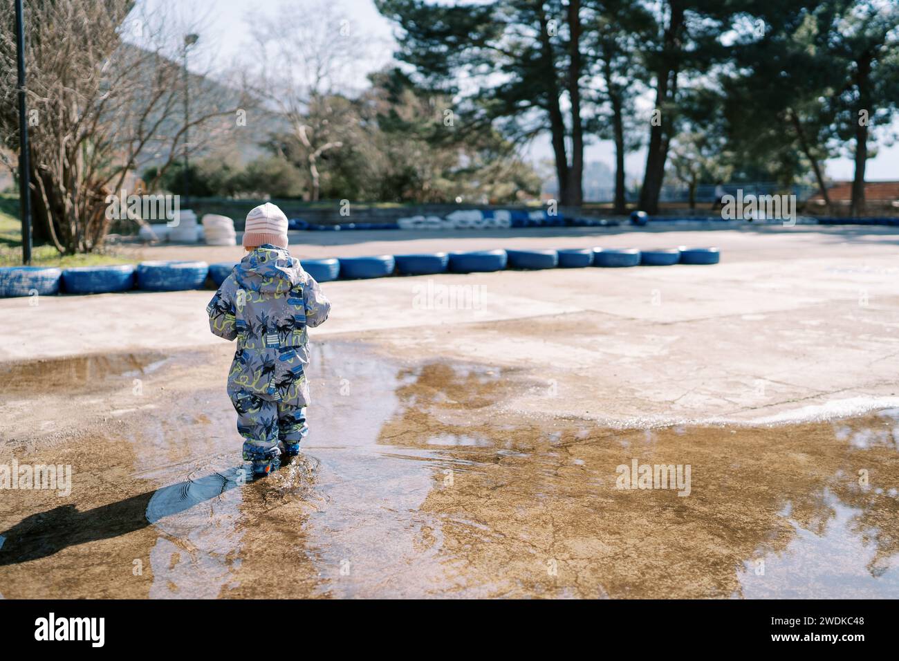 Little girl walks through a puddle on the playground towards a row of ...