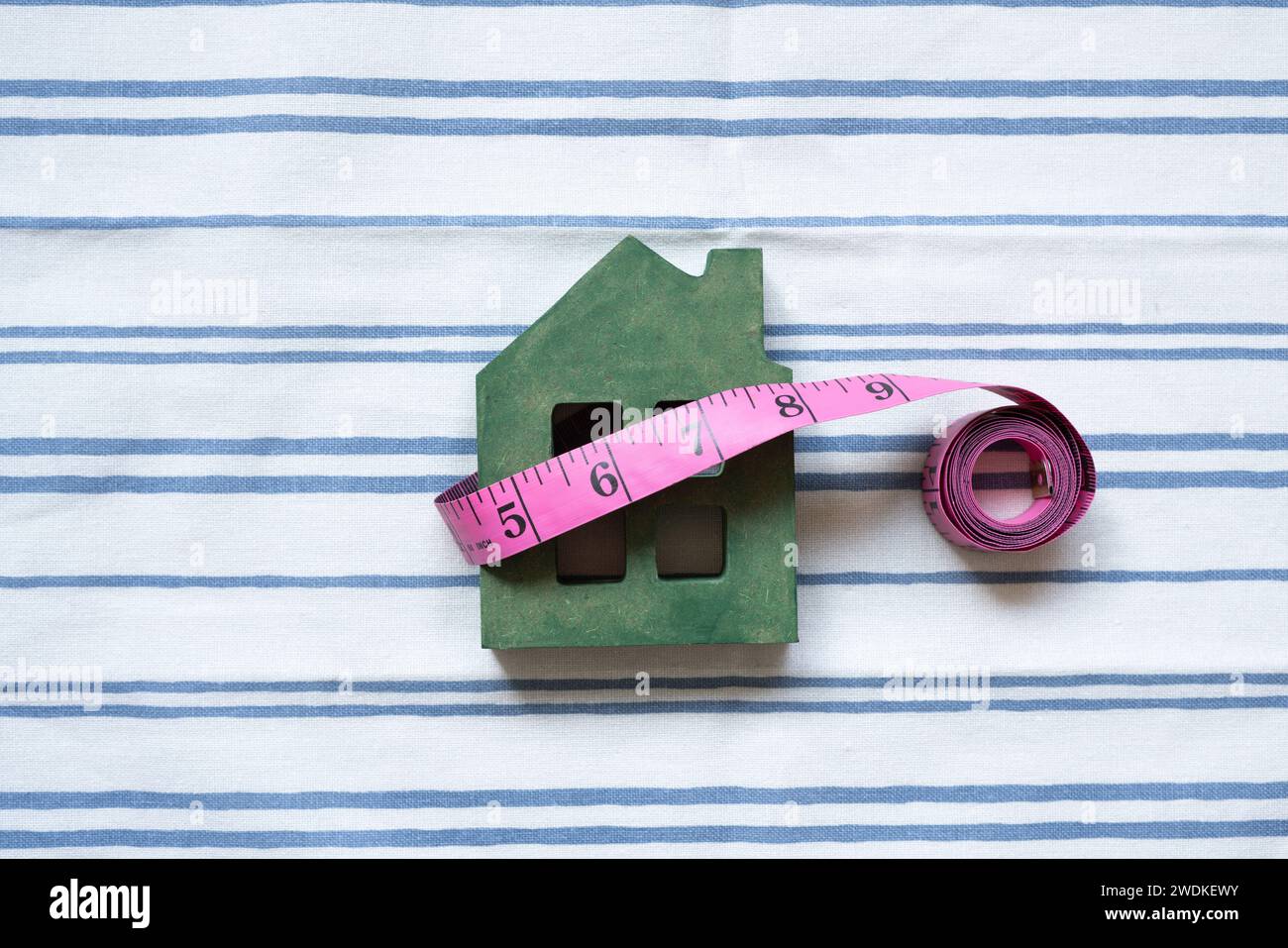 Miniature green model house and tape measure on stripe pattern fabric ...