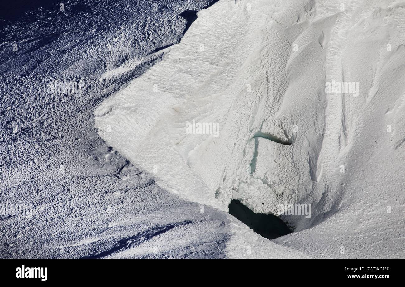 A deep crevasse with a pool with frozen and crusted snow on the rim, on ...