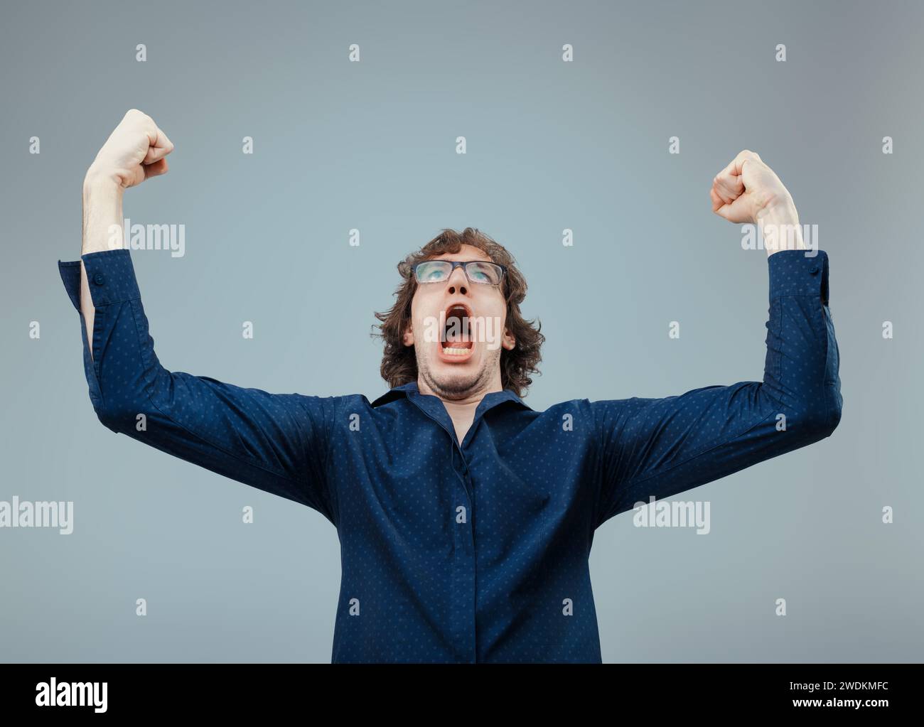 Exuberant man celebrates with arms raised, eyes wide and mouth open in ...