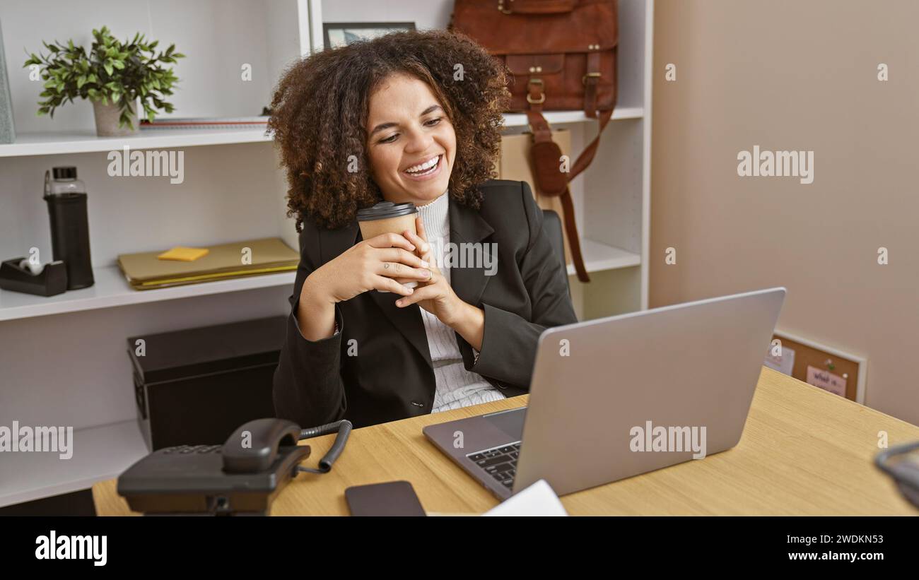 Hispanic curly-haired young woman enjoying coffee in a modern office ...