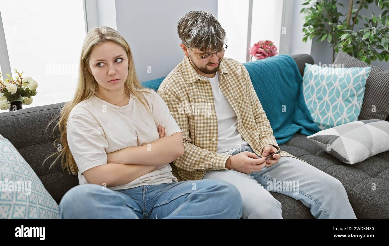 A displeased woman and a distracted man sit together but emotionally ...