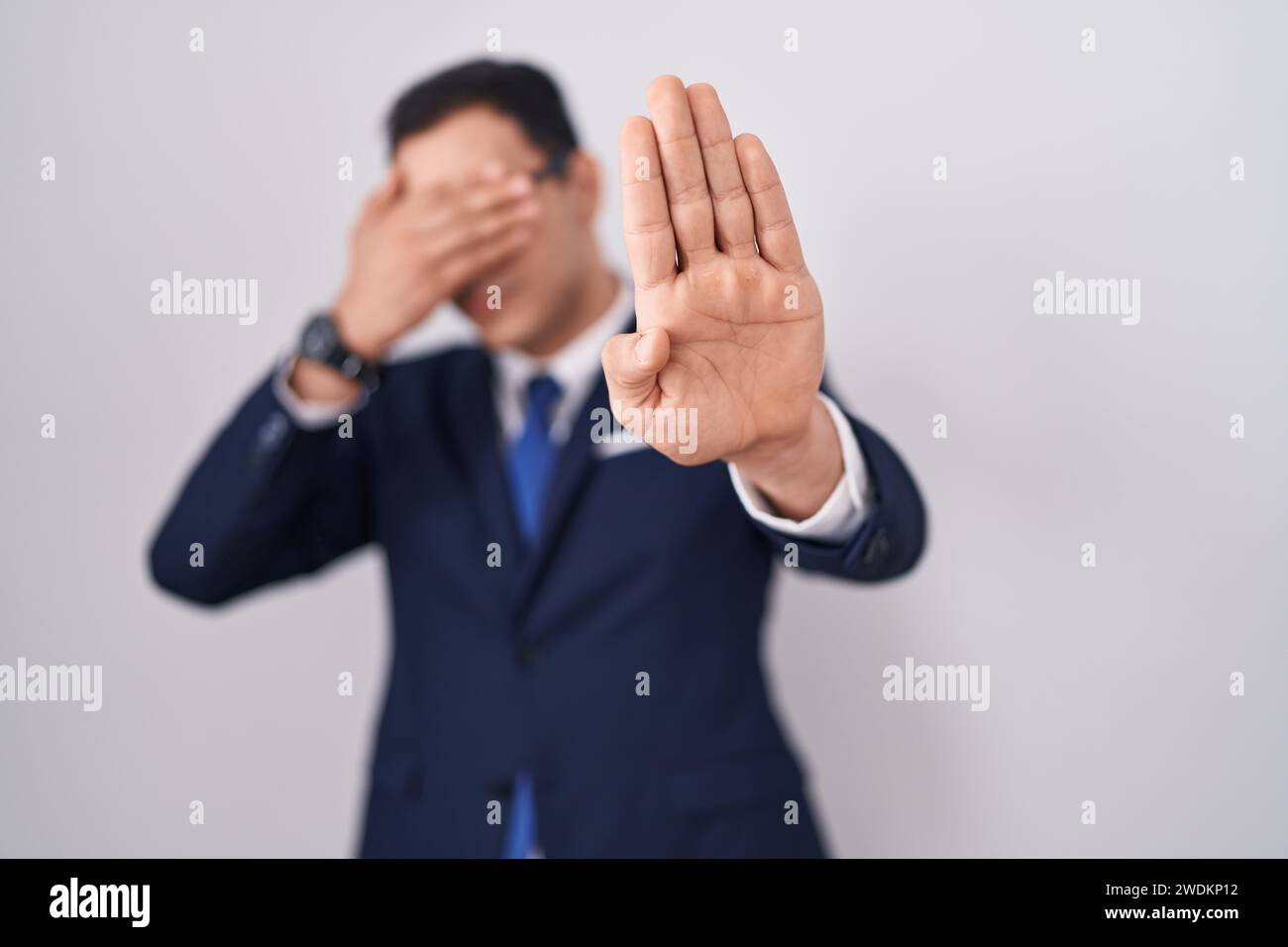Young hispanic man wearing suit and tie covering eyes with hands and ...
