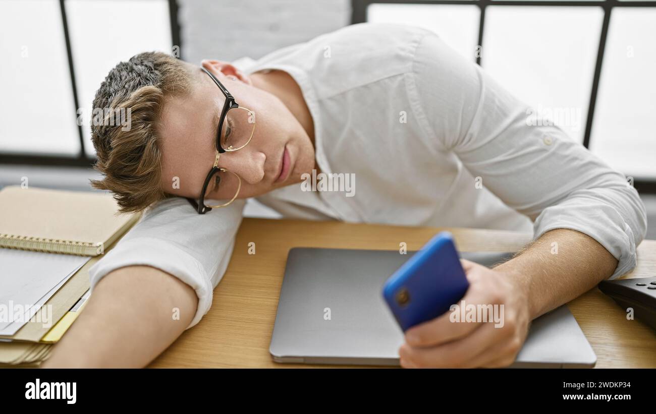 Exhausted young caucasian businessman, smartphone in hand, loses battle ...
