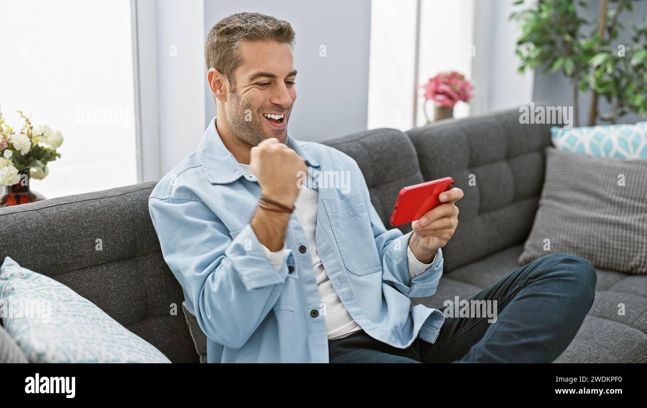 A cheerful man reacts positively while using a smartphone in a cozy ...