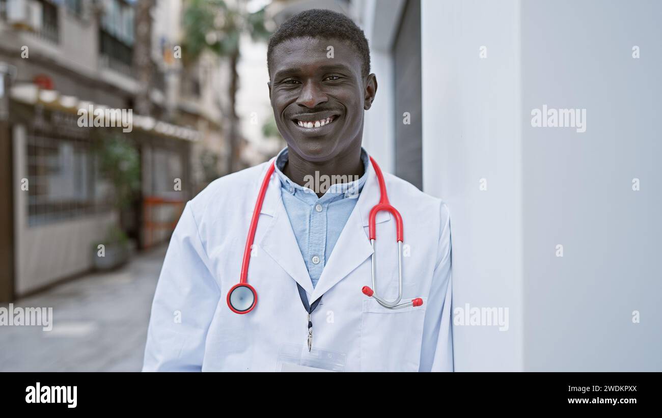 Smiling african man in white lab coat with red stethoscope on urban ...