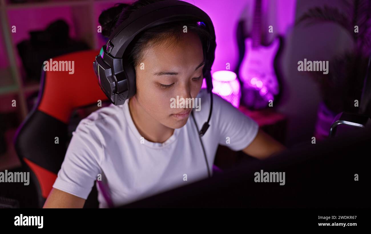 Concentrated asian woman gaming in a dark room with colorful lighting ...
