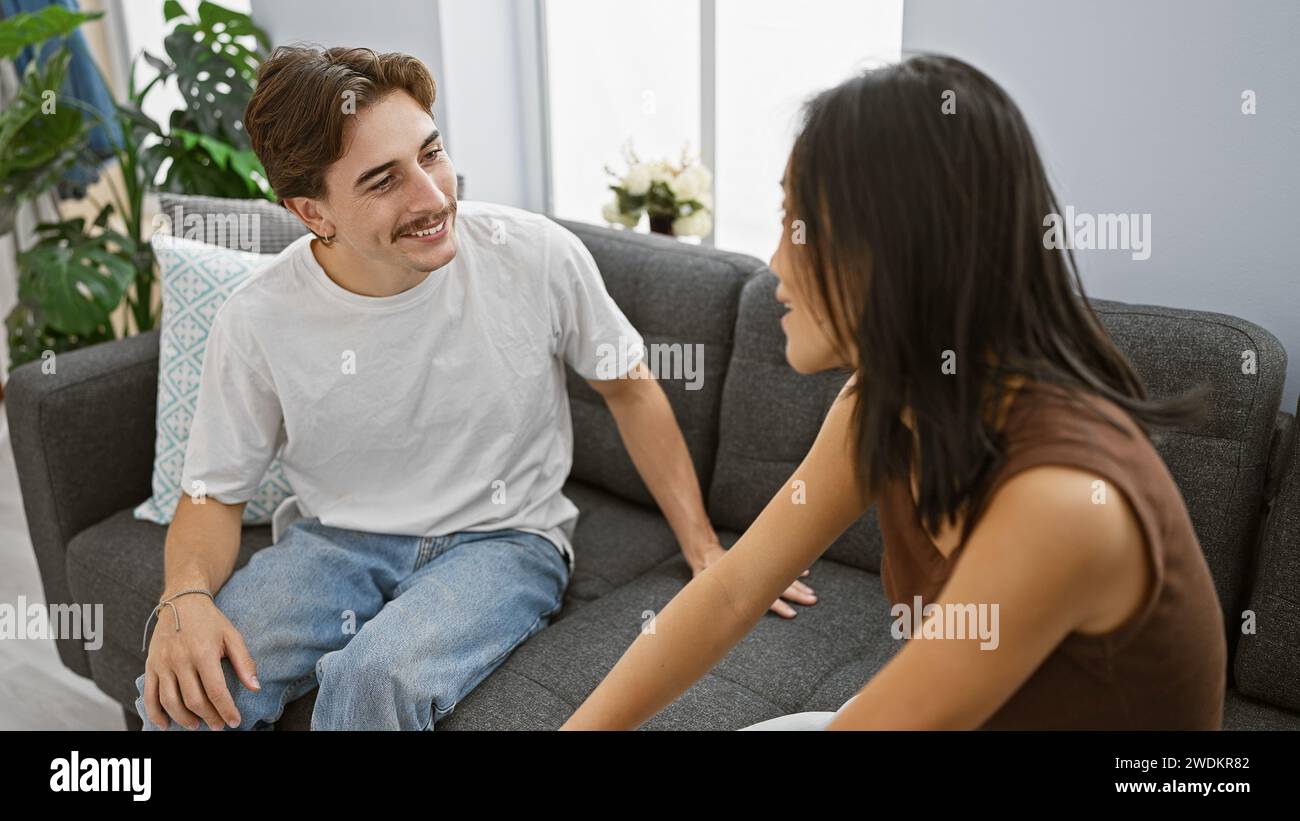 A man and woman sit closely on a sofa in their modern apartment ...