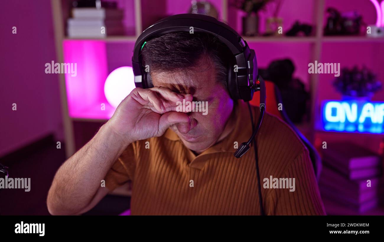 Stressed middle-aged man with headphones in dark gaming room looks ...