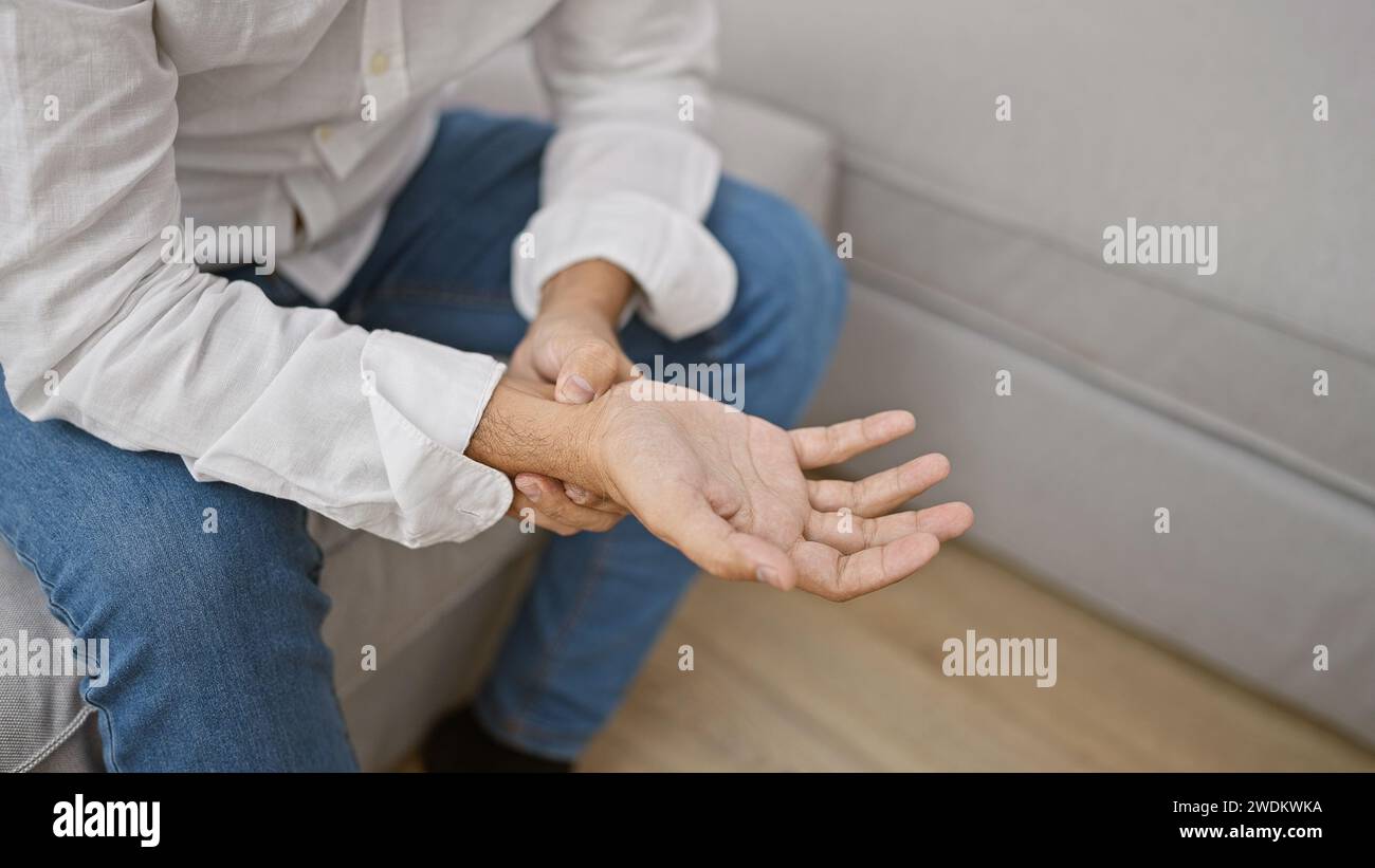Worried young hispanic man with grey hair, enduring wrist pain at home ...