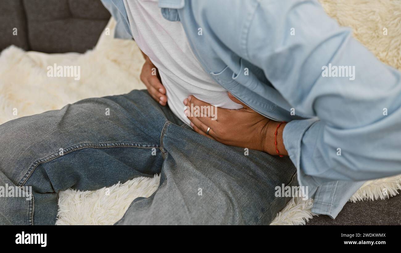 A man experiencing abdominal pain while sitting on a couch indoors ...